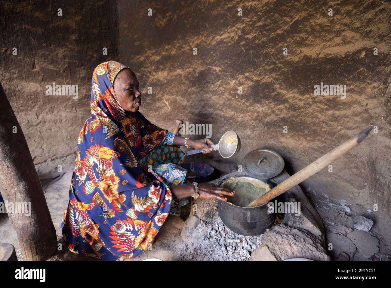 An elderly woman cooks a traditional meal of millet paste over a fire ...