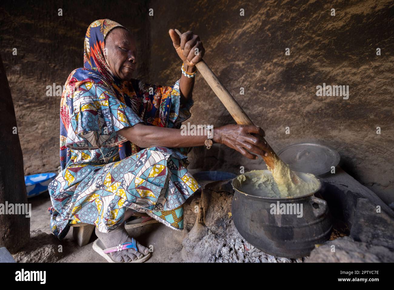 An elderly woman cooks a traditional meal of millet paste over a fire ...