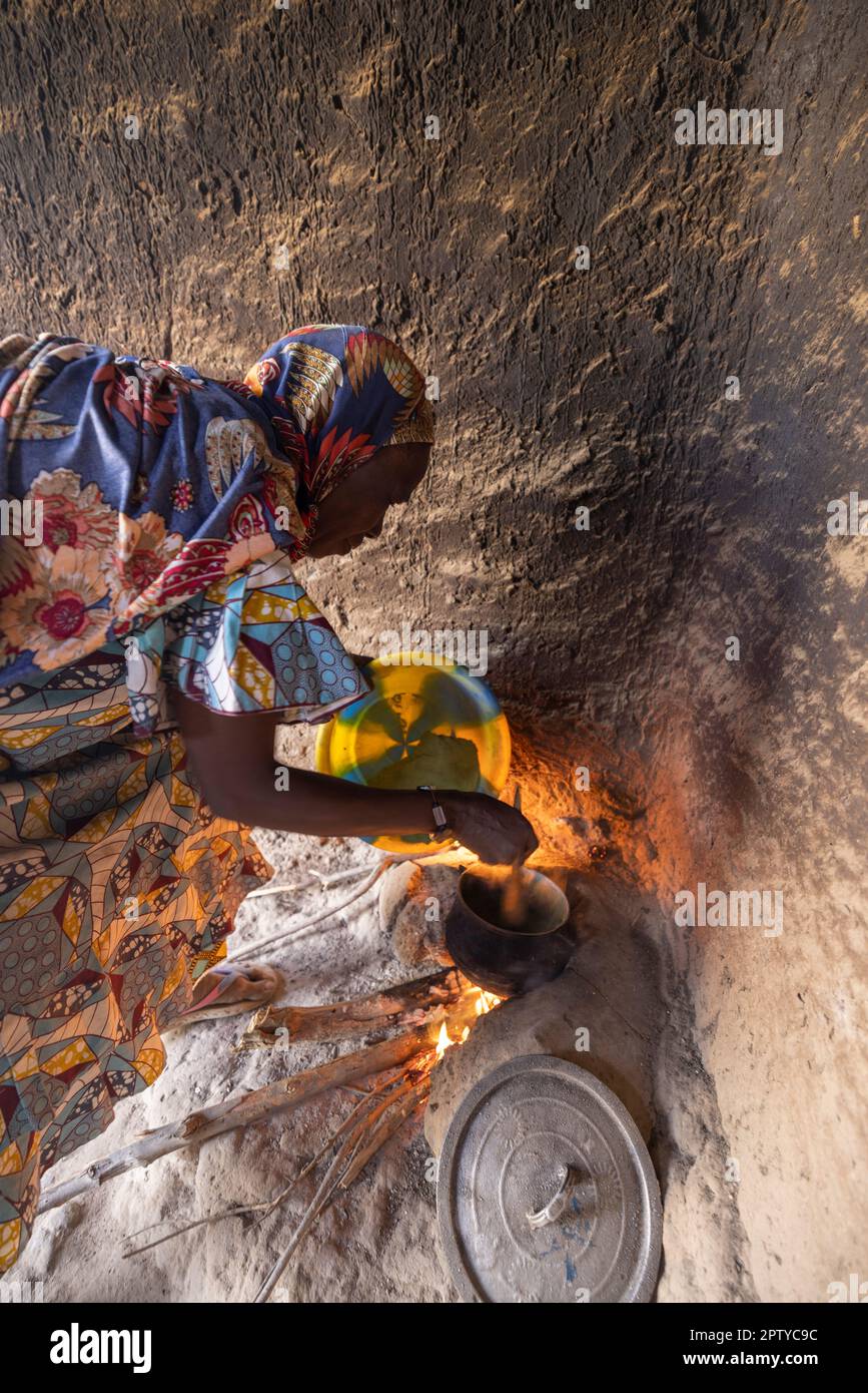 An elderly woman cooks a traditional meal of millet paste over a fire ...