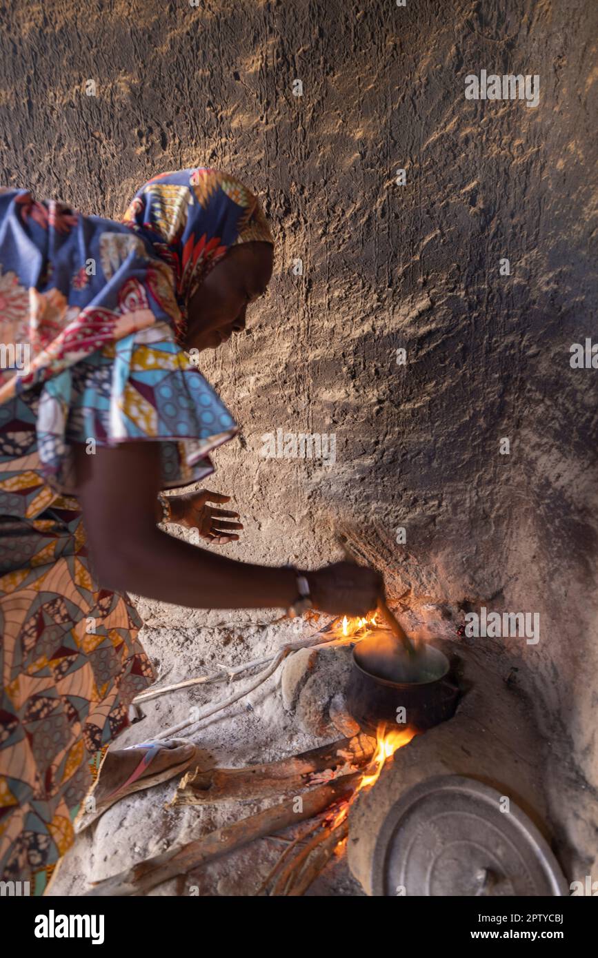 An elderly woman cooks a traditional meal of millet paste over a fire ...