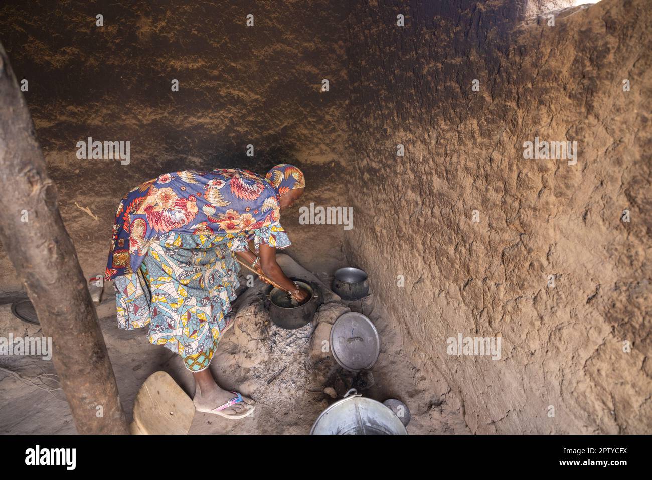 An elderly woman cooks a traditional meal of millet paste over a fire ...