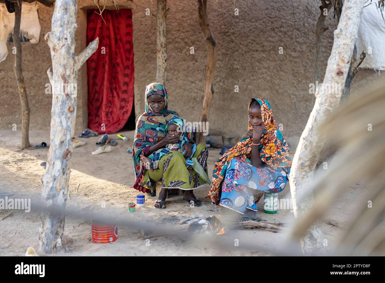 Sisters from the Fulani tribe, one carrying a baby, warm themselves by ...