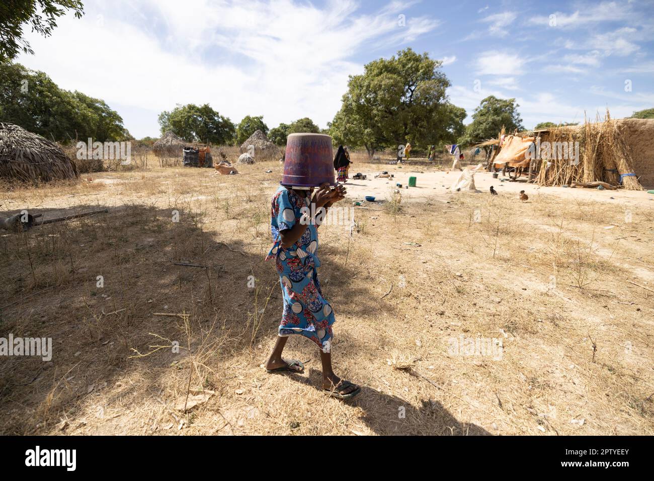A girl walks through a dry, arid landscape with a bucket on her head in ...