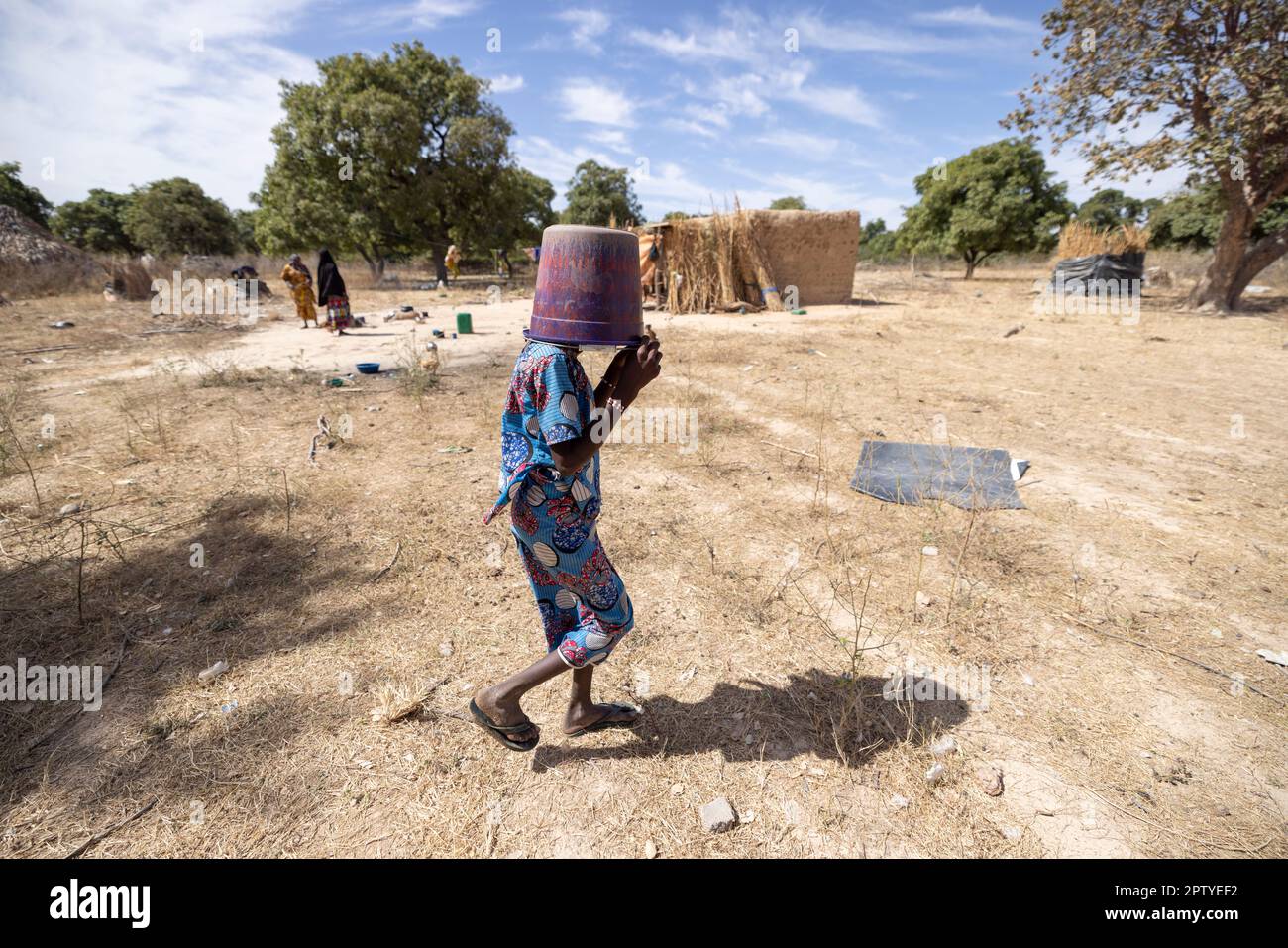A girl walks through a dry, arid landscape with a bucket on her head in ...
