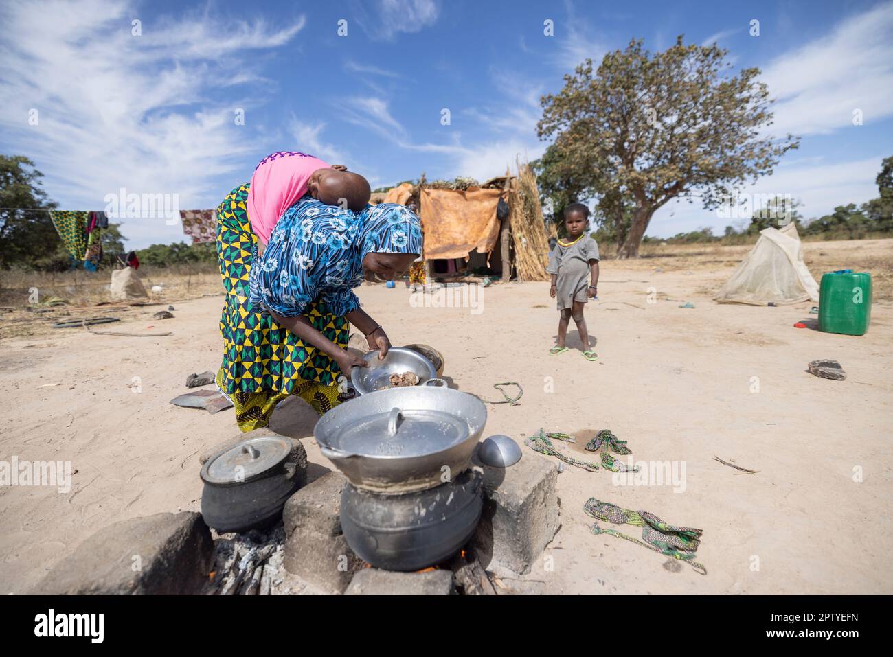 Mother cooking a meal over an open fire in front of the family's home ...
