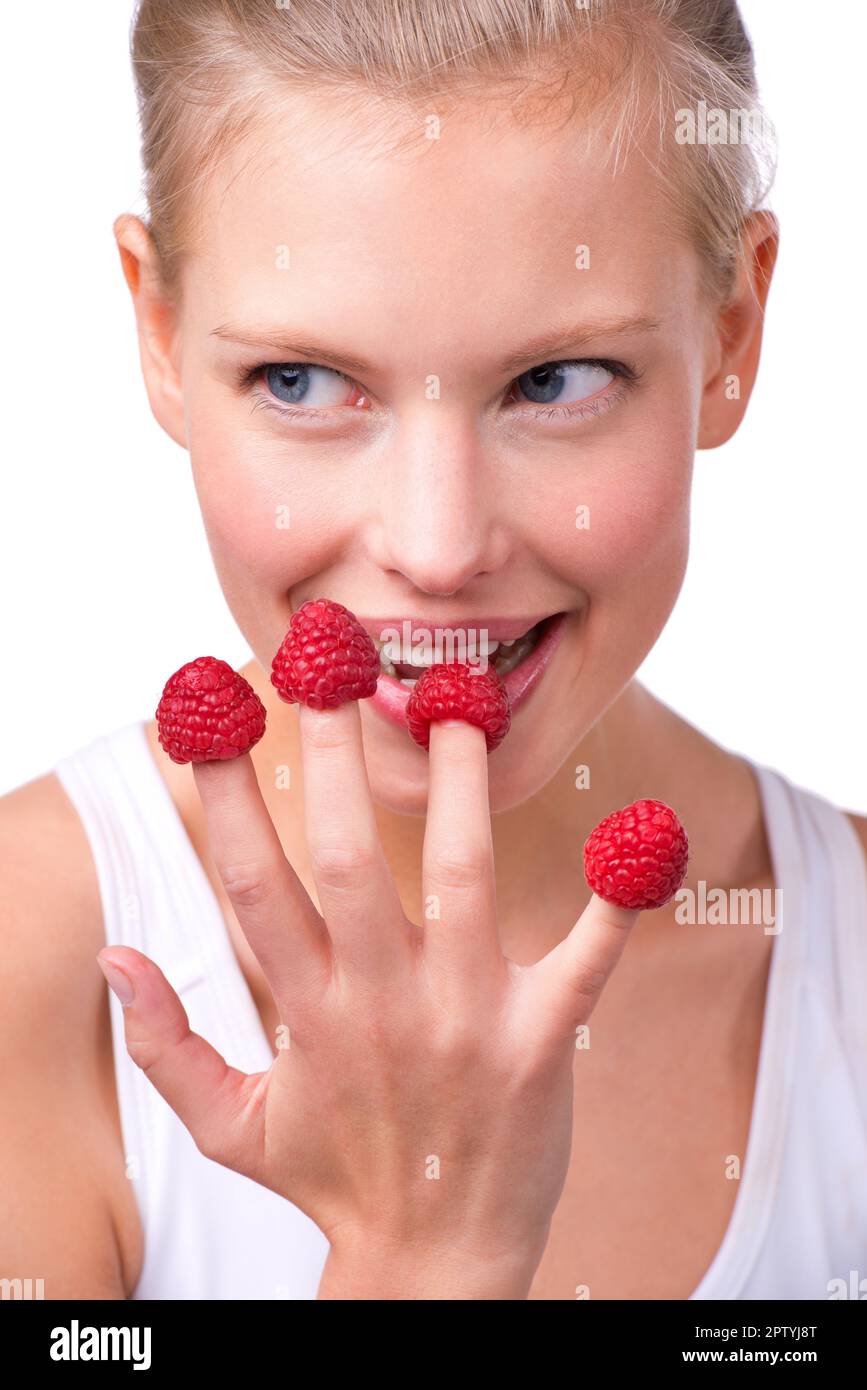 Finger food. a beautiful young woman playfully eating raspberries off ...