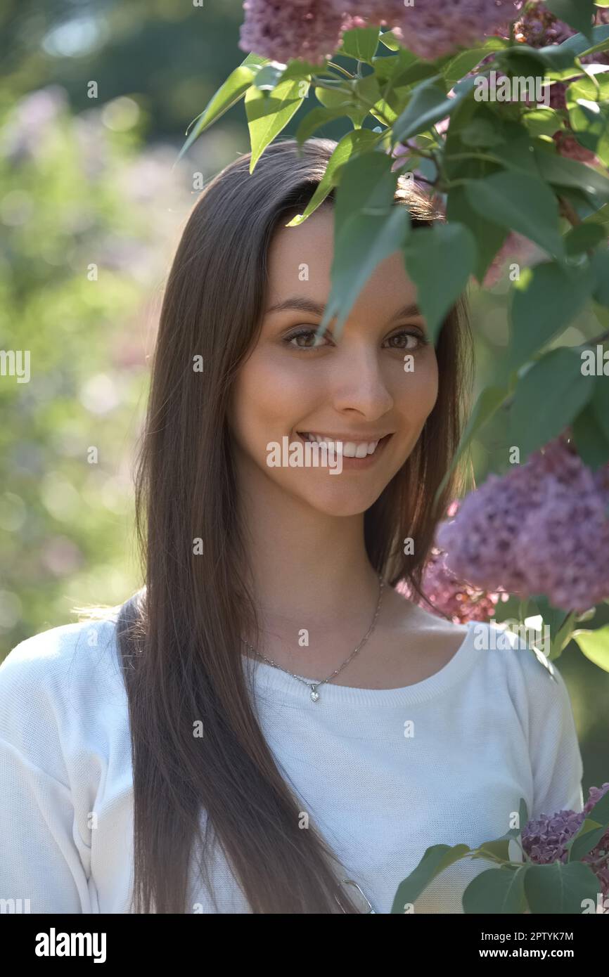 Outdoor portrait of beautiful smiling girl standing among lilac bushes ...