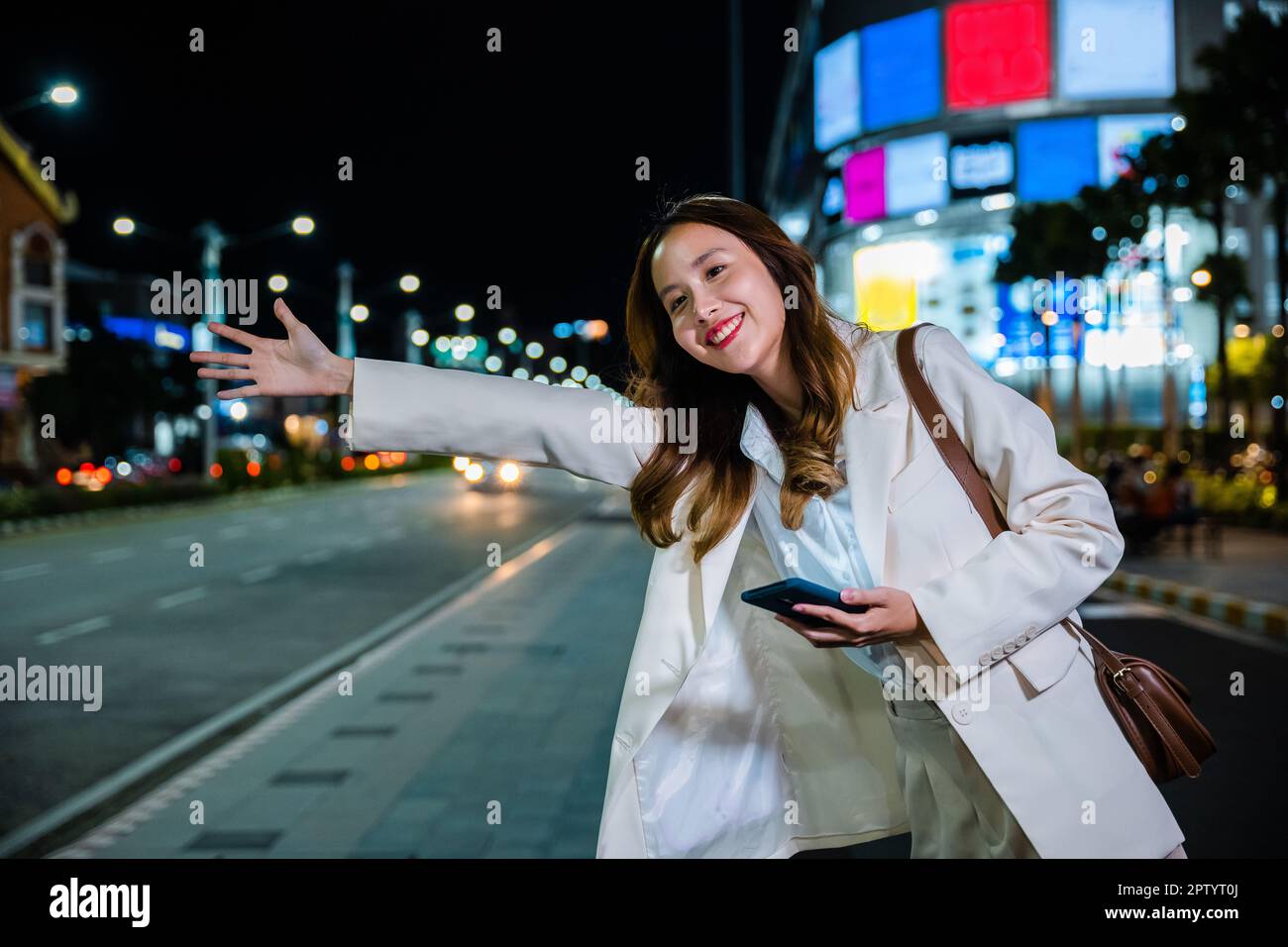 Asian businesswoman standing hail waving hand taxi on road in busy city street at night ...