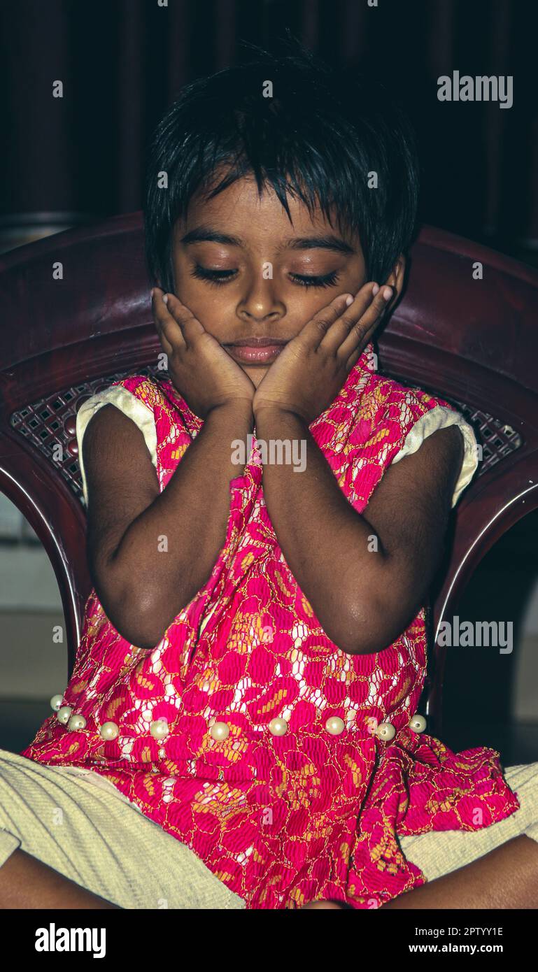 A little girl is feeling bad sitting in a chair with her hands over her ...