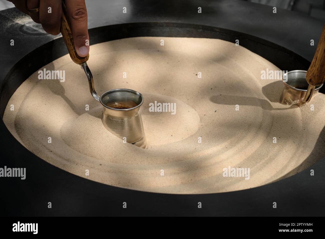 Close-up of turkish coffee making in cezve on sand in coffee bar. A ...
