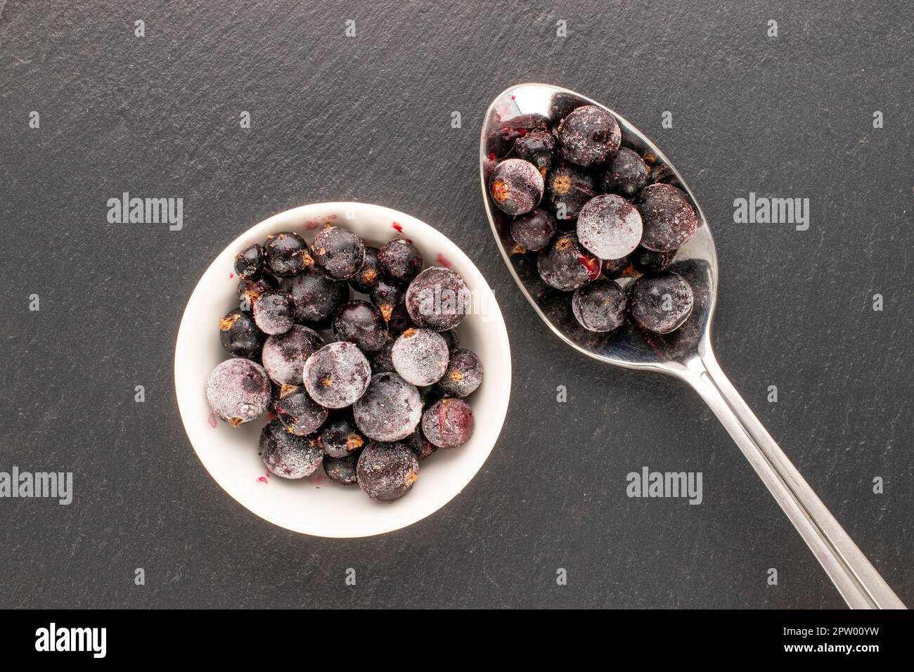 Frozen black currant with white saucer and metal spoon on slate stone ...