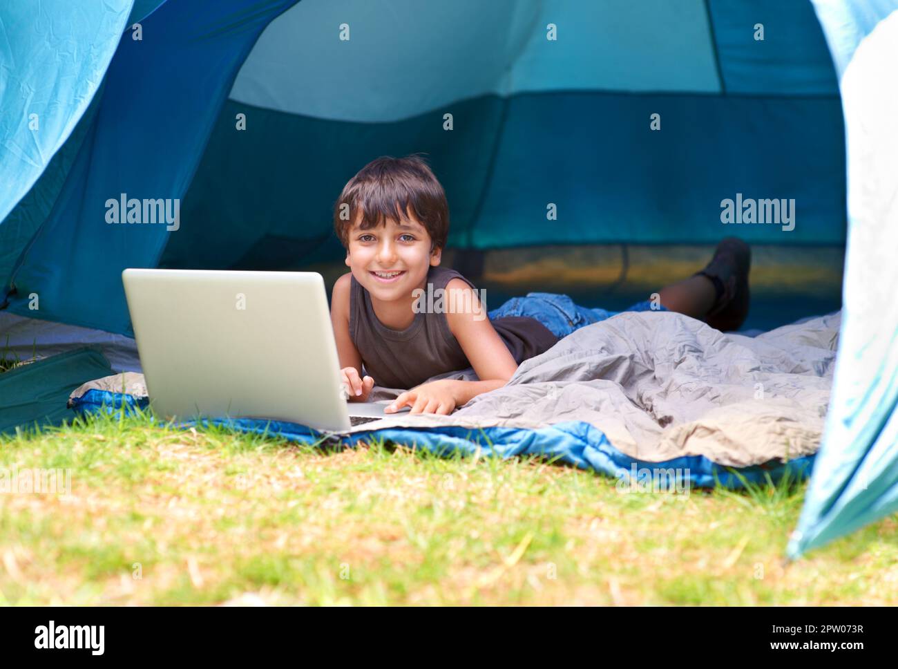 Digital fun in the great outdoors. A young boy using a laptop while ...