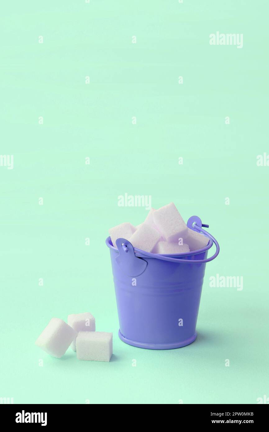 A miniature lilac bucket filled with cubes of sugar lies on a turquoise ...