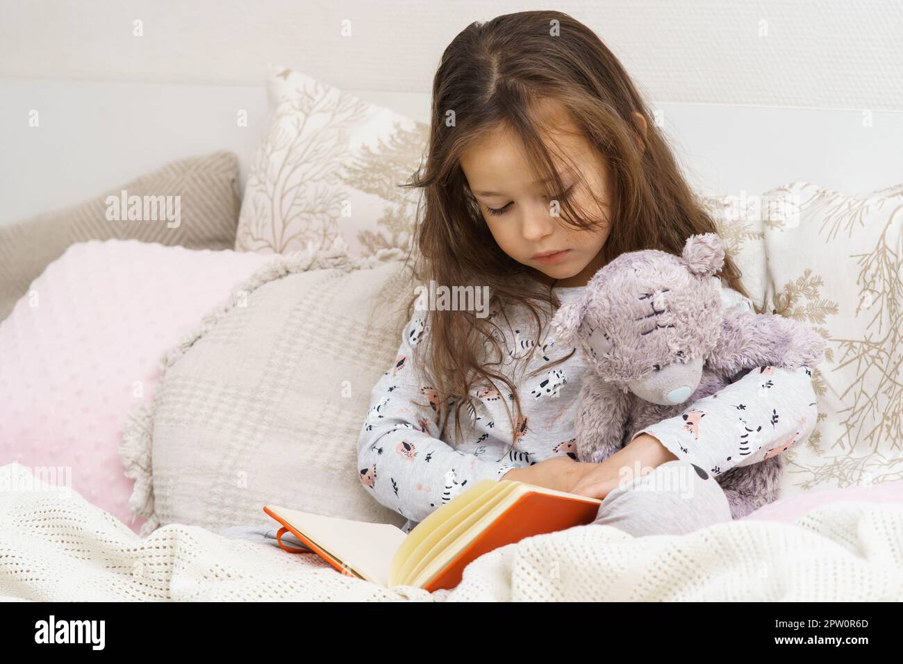 Little pensive, nice lonely brunette girl in pajamas reading book with ...