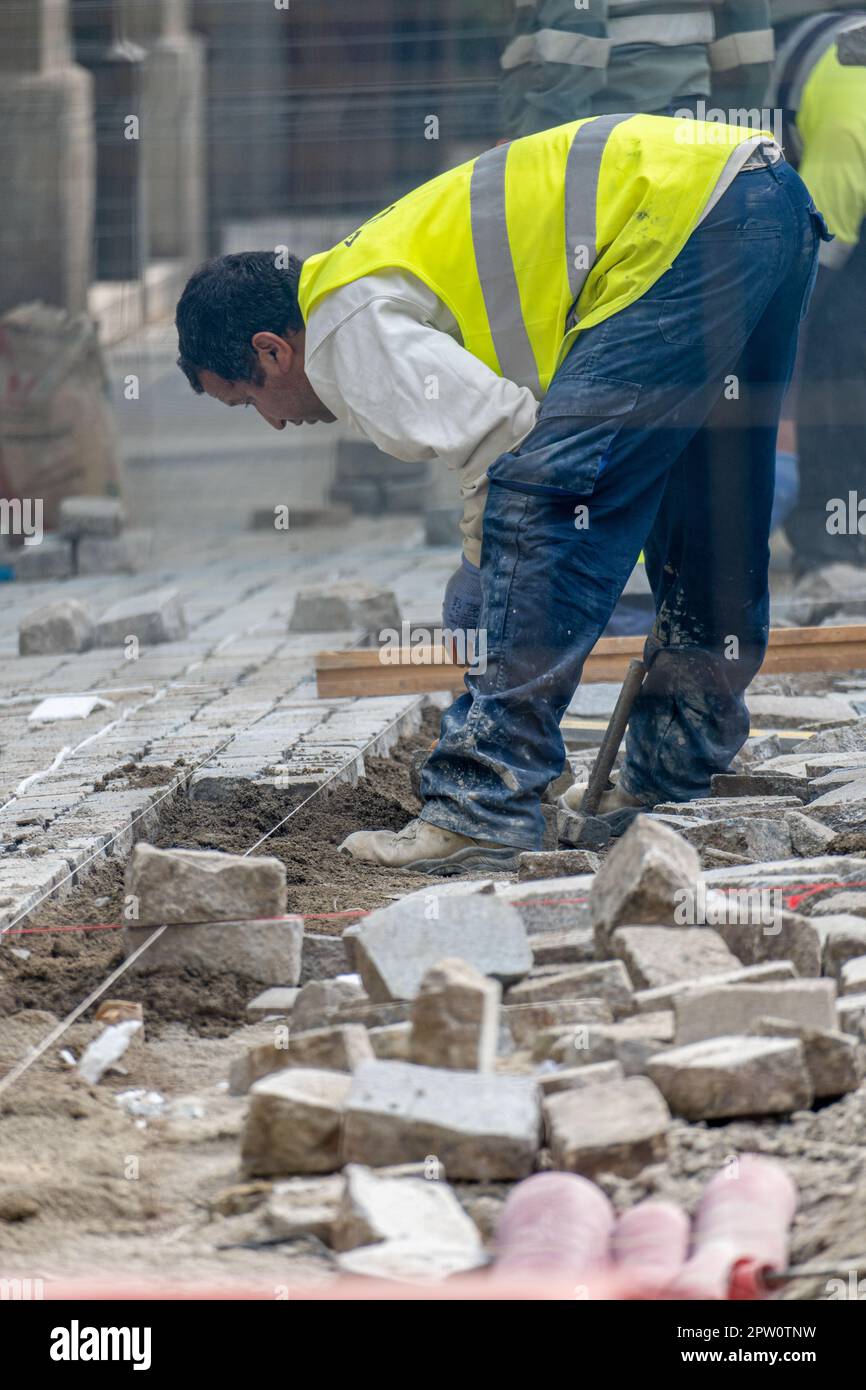 Worker laying interlocking pavers during sidewalk construction with ...