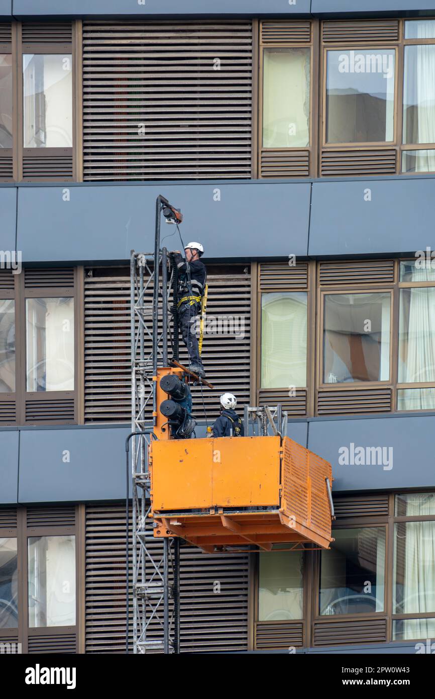 Maintenance workers on a hanging cradle or lifting platform carrying ...