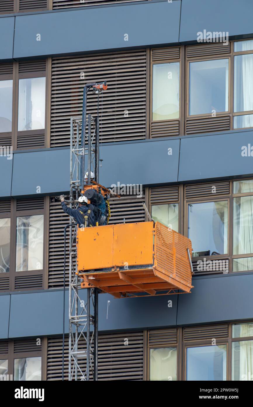 Maintenance workers on a hanging cradle or lifting platform carrying ...
