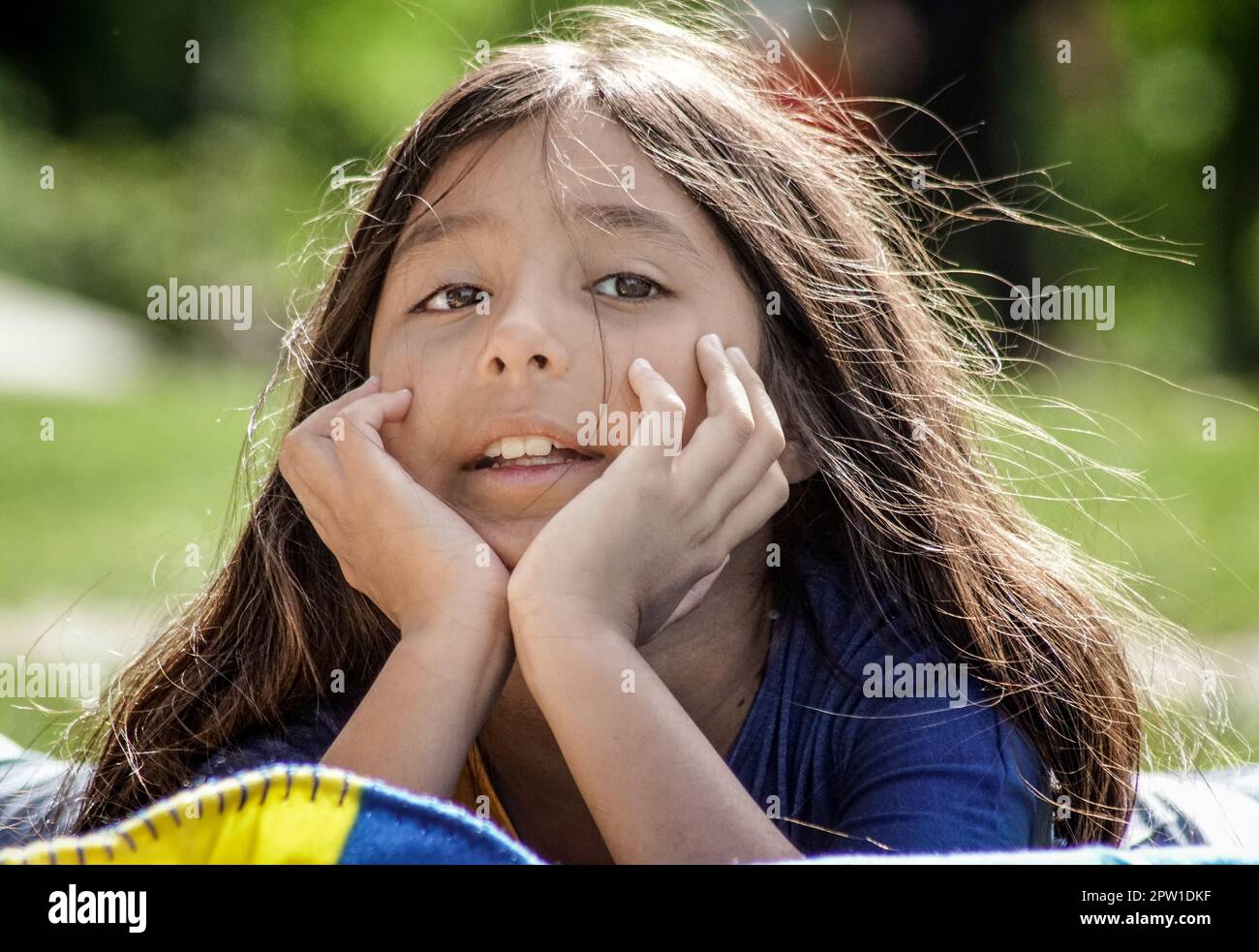 Close-up portrait of cute girl with hands on chin lying on field Stock ...