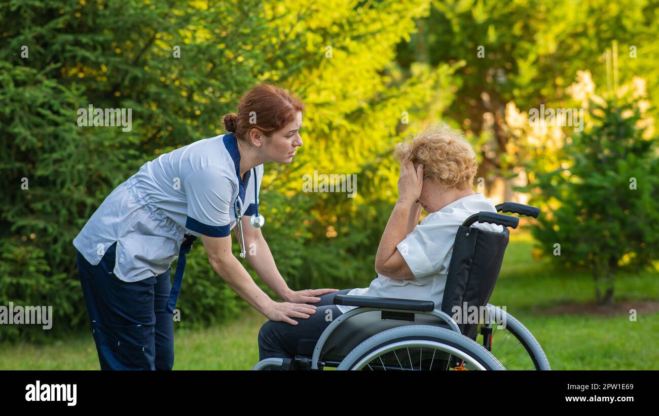 A nurse comforts a crying elderly caucasian woman in a wheelchair ...