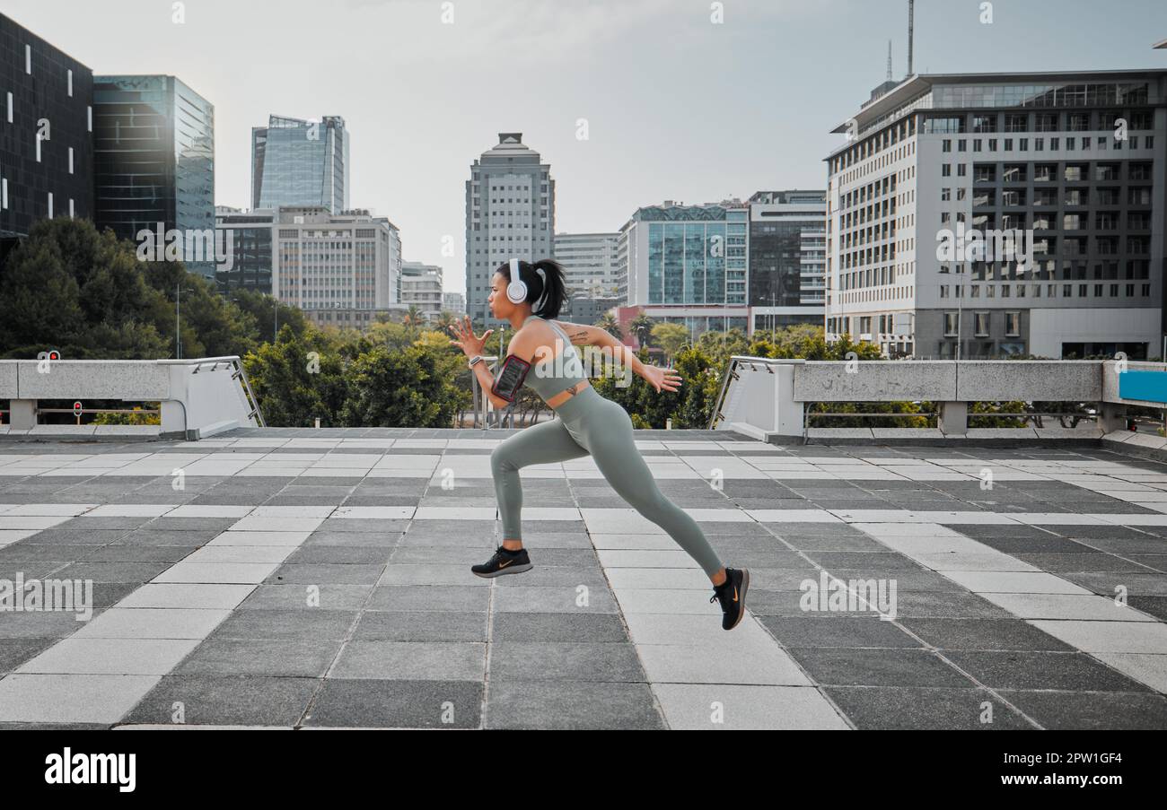 Young mixed race hispanic female wearing headphones listening to music and running outside in ...