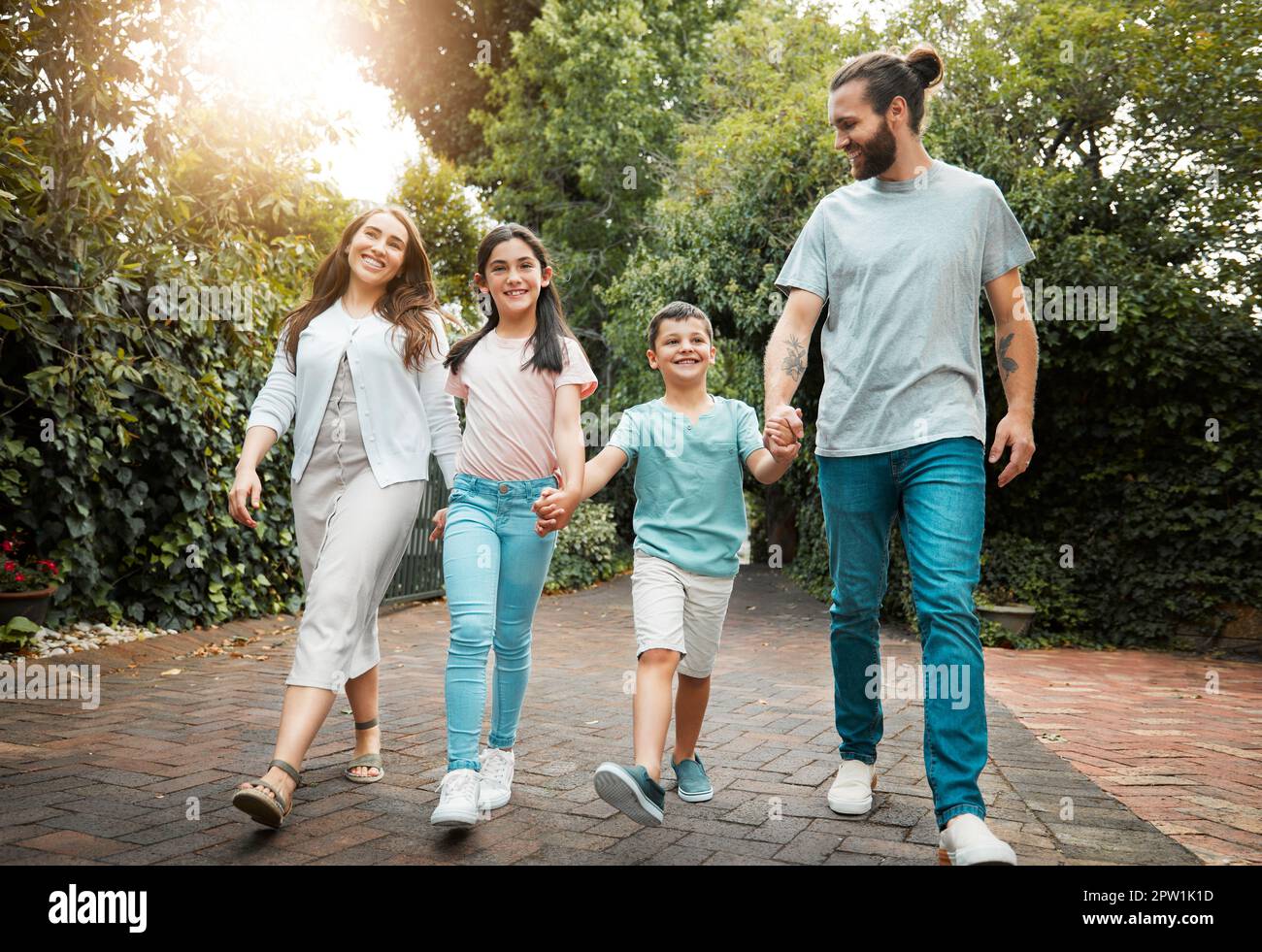 Happy young caucasian family of four holding hands and going for a walk in the neighbourhood ...