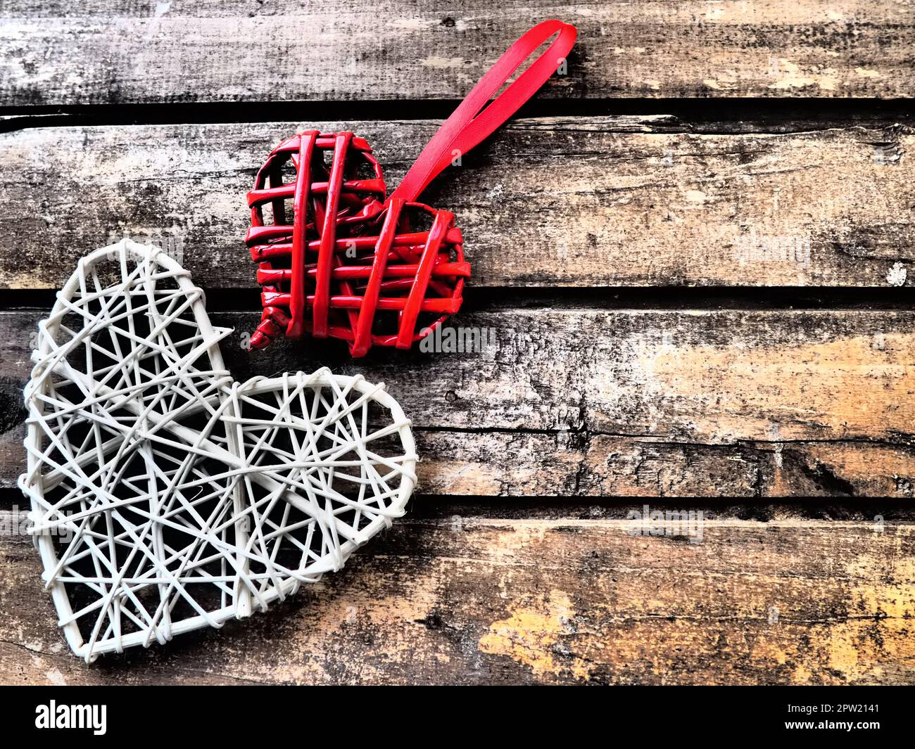 A wicker hearts a wooden background. Two red braided heart with hanging loop. White big heart ...