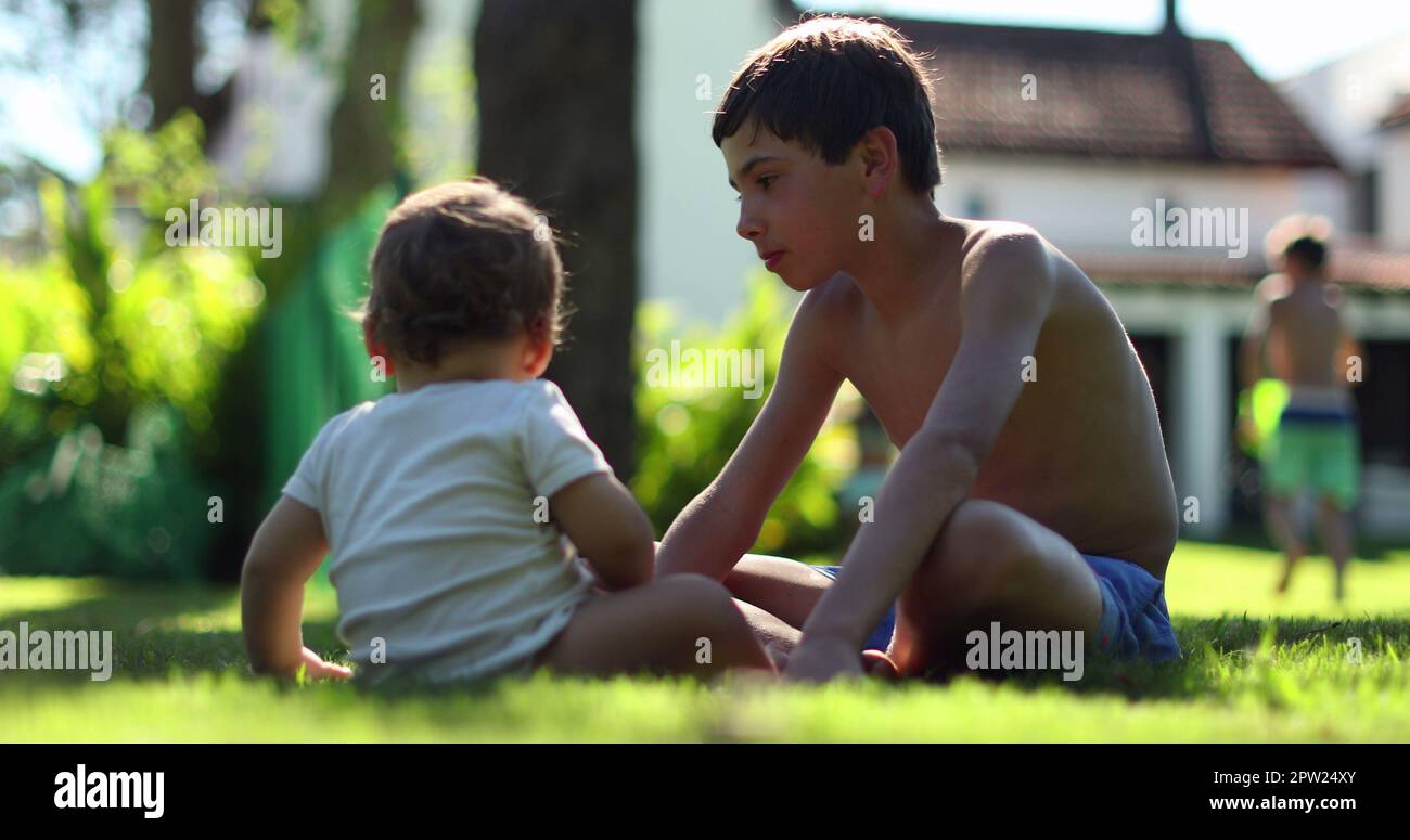 Brother interacting with baby sibling outside in backyard. Older ...