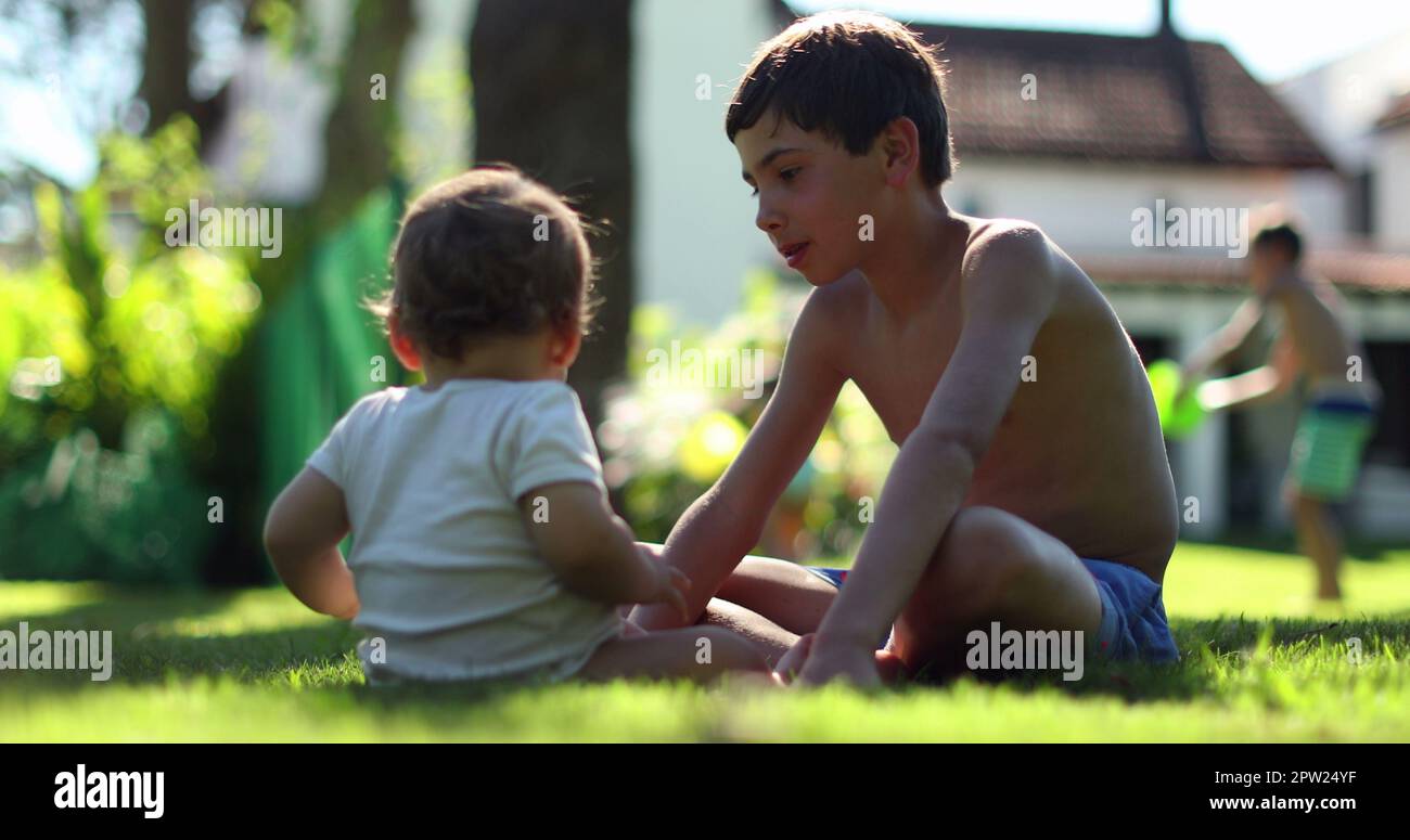 Brother interacting with baby sibling outside in backyard. Older ...