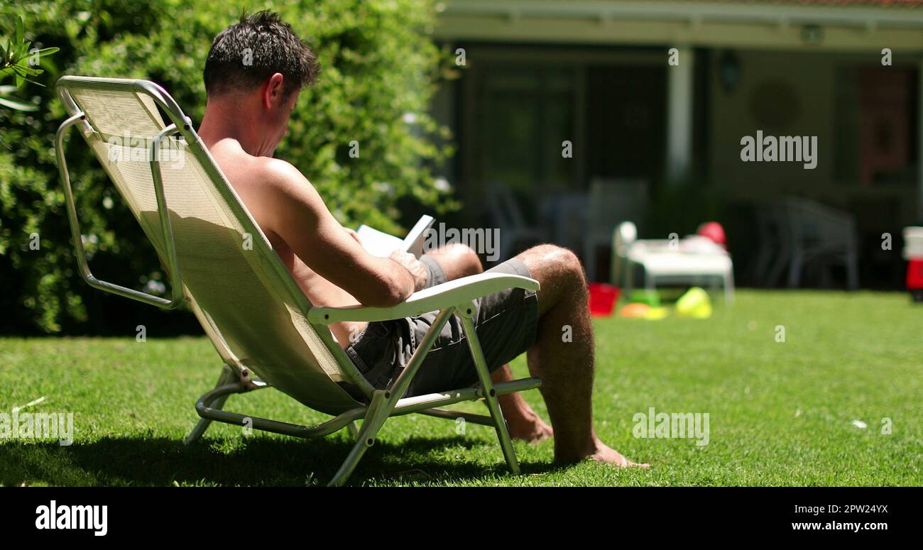 Candid man resting outside reading book during summer day. Person ...