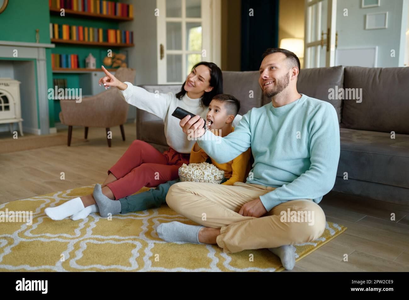 Amazed parents and curious kid watching tv program sitting on floor in ...