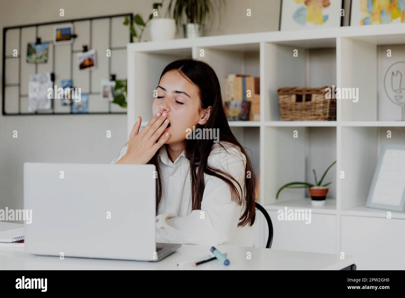 Tired brunette girl yawns tiredly with eyes closed while working with ...