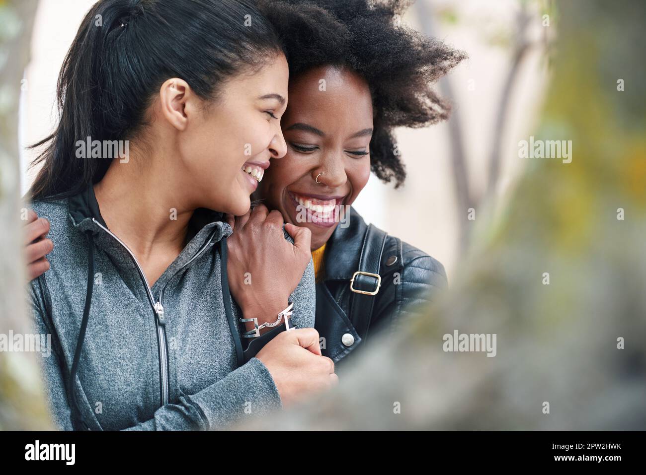 Two cheerful friends hugging one another and laughing during a trip to the park. A happy young ...
