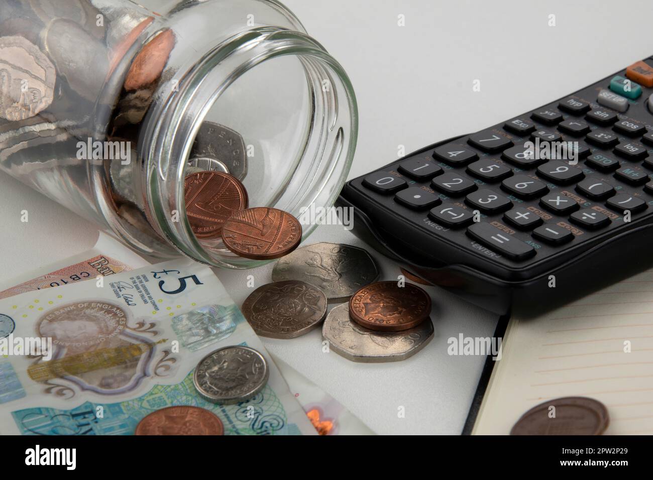 Glass bottle fallen over, spilling coins onto white table with ...
