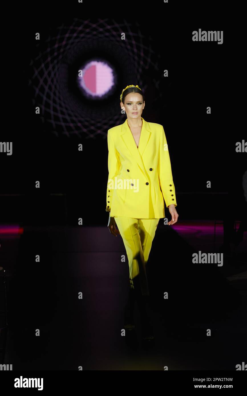 Fashion model walks the runway in yellow pantsuit, on her background ...