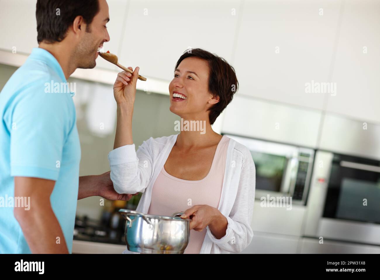 Here, have a taste. a woman giving her husband a taste of the food shes ...