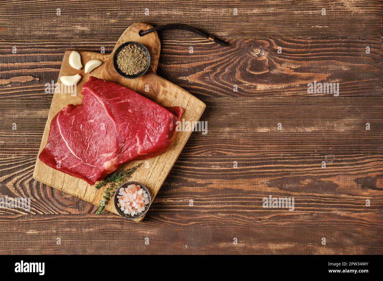 Overhead view of raw top side beef steak on wooden tabletop with place ...