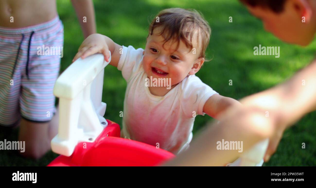 Baby having fun outside pushing car toy with siblings. Smiling toddler ...