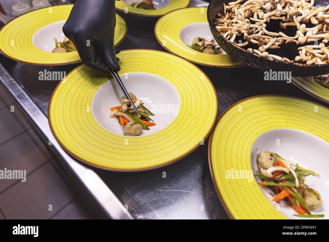 Chef decorating a dish with shimeji mushrooms in restaurant kitchen ...