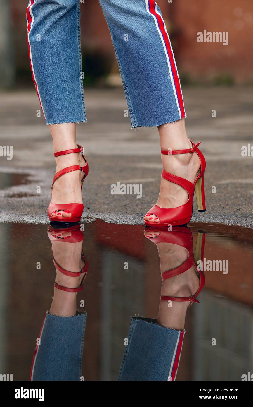 Reflection of female legs in jeans and red shoes in puddle on asphalt ...