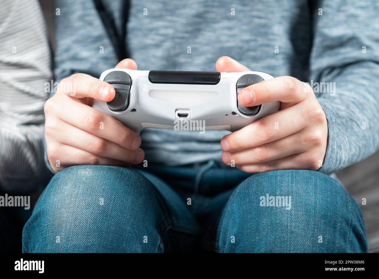Unrecognizable teenage boy child sitting at home, holding white gaming ...
