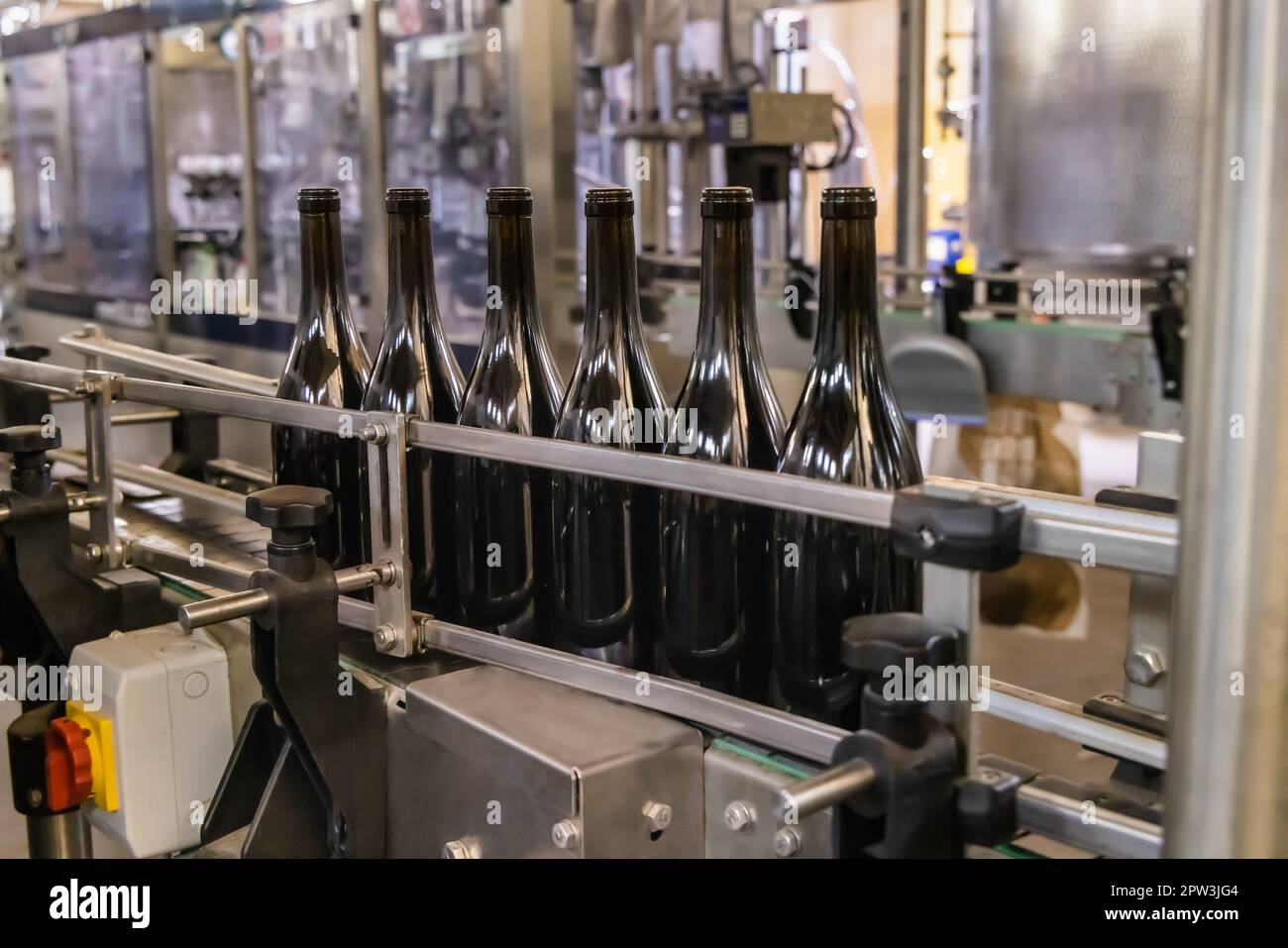 Dark glass bottles being filled with wine by industrial bottling ...
