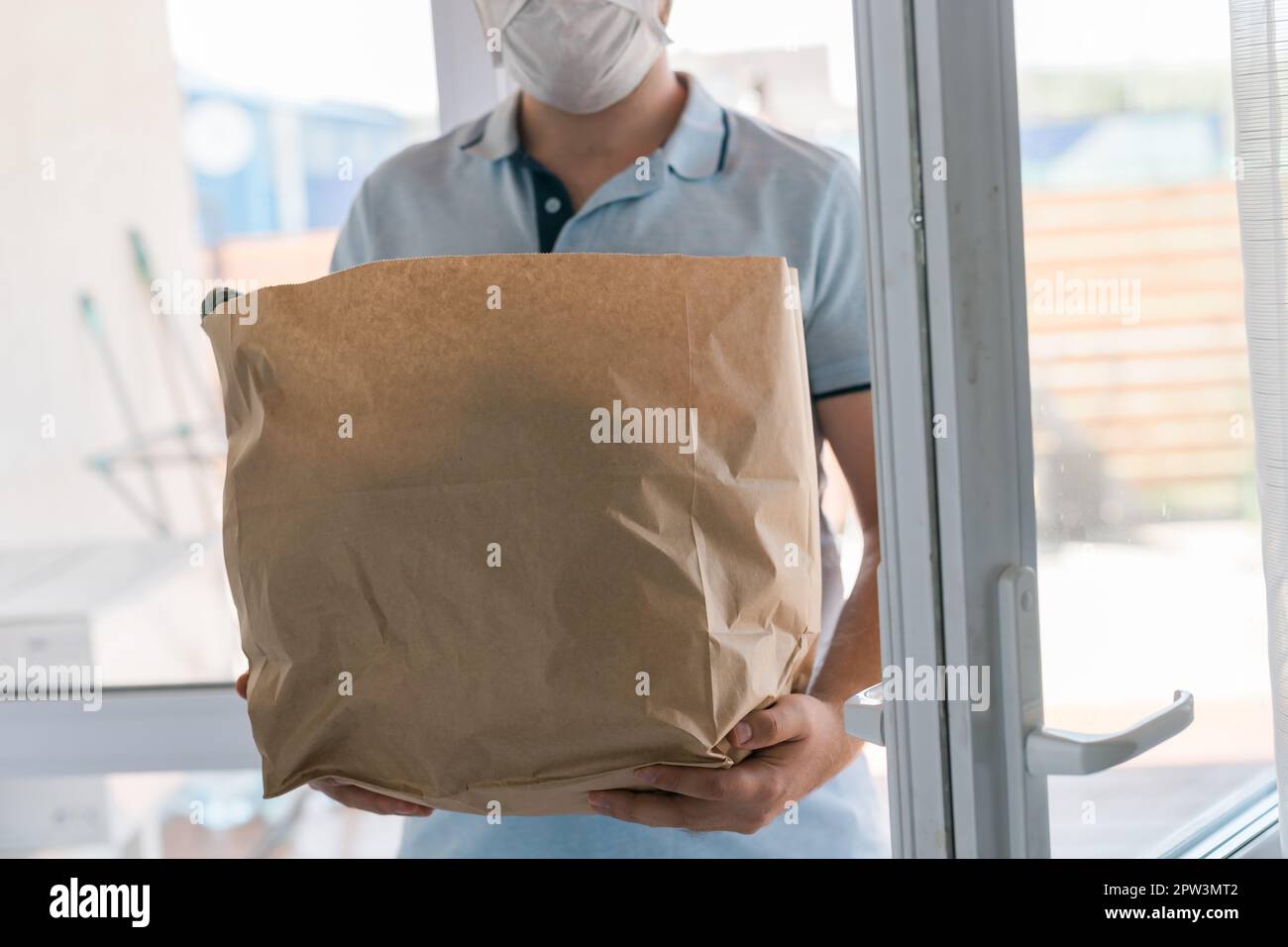 Deliver man wearing face mask in blue uniform handling bag of food give ...