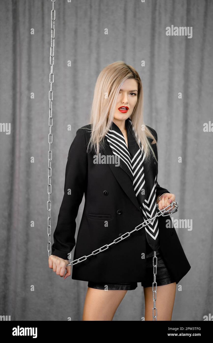 Strong woman in black jacket and leather shorts holds metal chain in ...