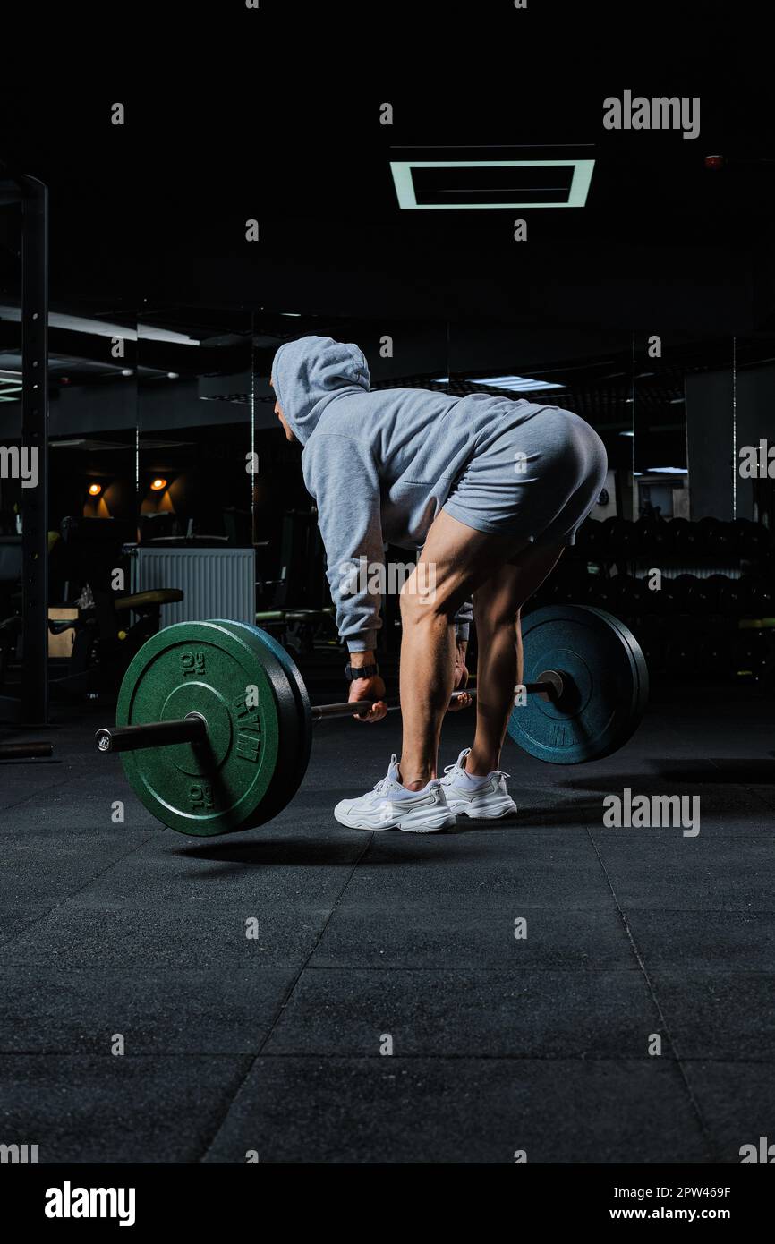 Muscular man doing deadlift exercise with barbell in gym, side view ...
