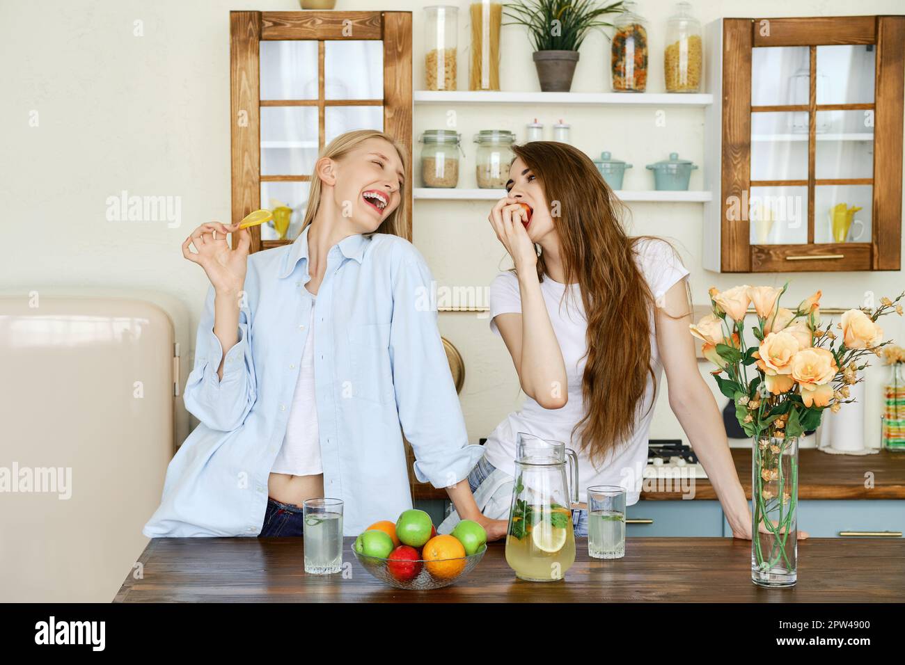 Two beautiful young women eat fruits in the kitchen Stock Photo - Alamy
