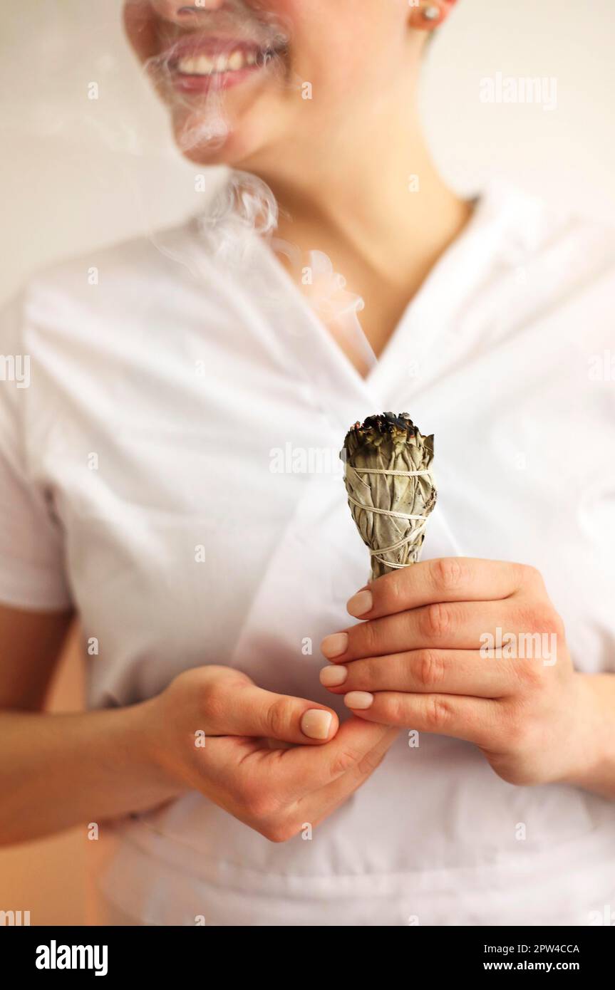 Unrecognizable female burning sage smudge stick and smelling smoke ...