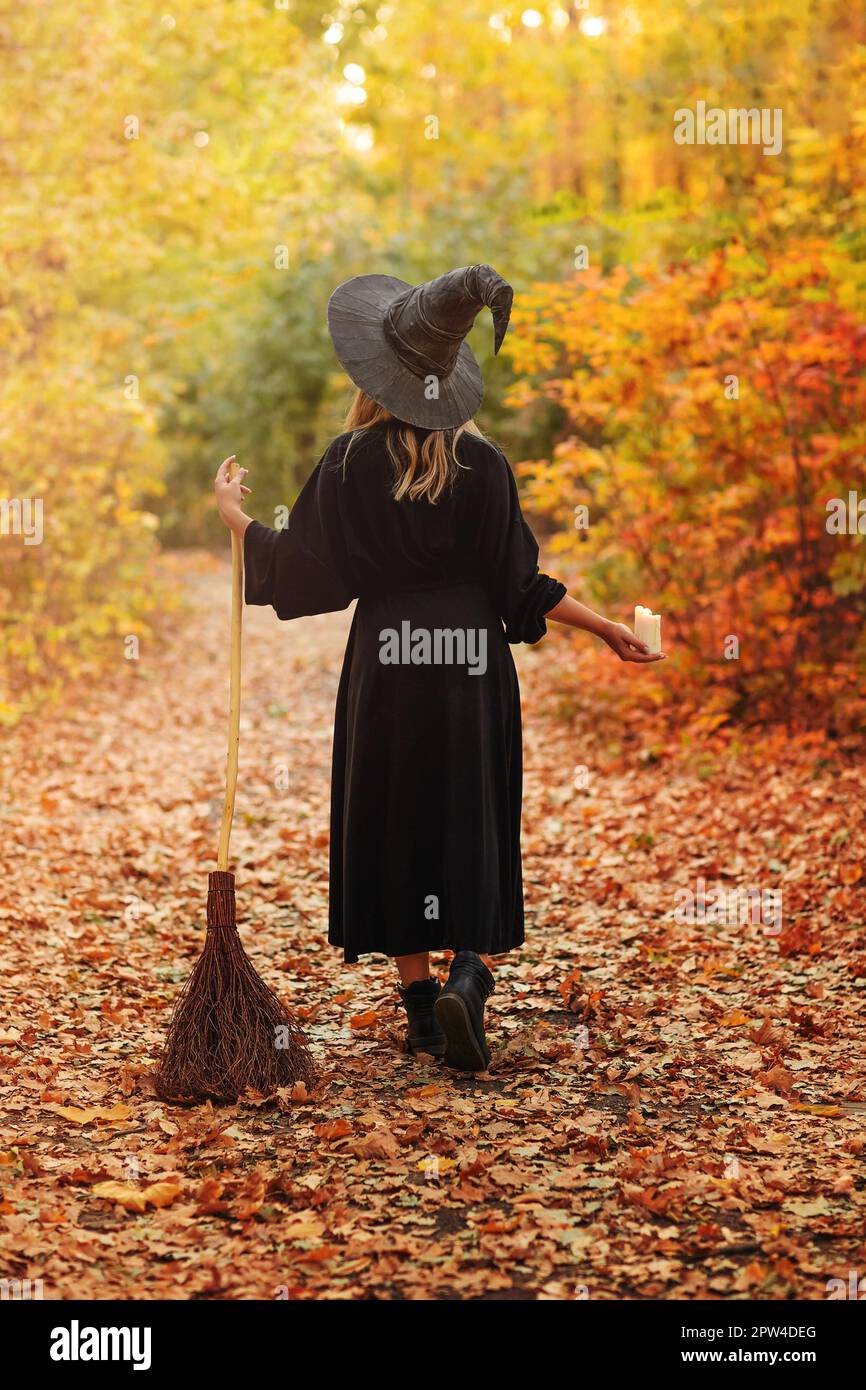Back view of anonymous woman in witch costume with broom walking on ...