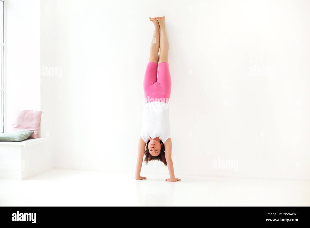 Full body of focused slim female female performing handstand near wall ...
