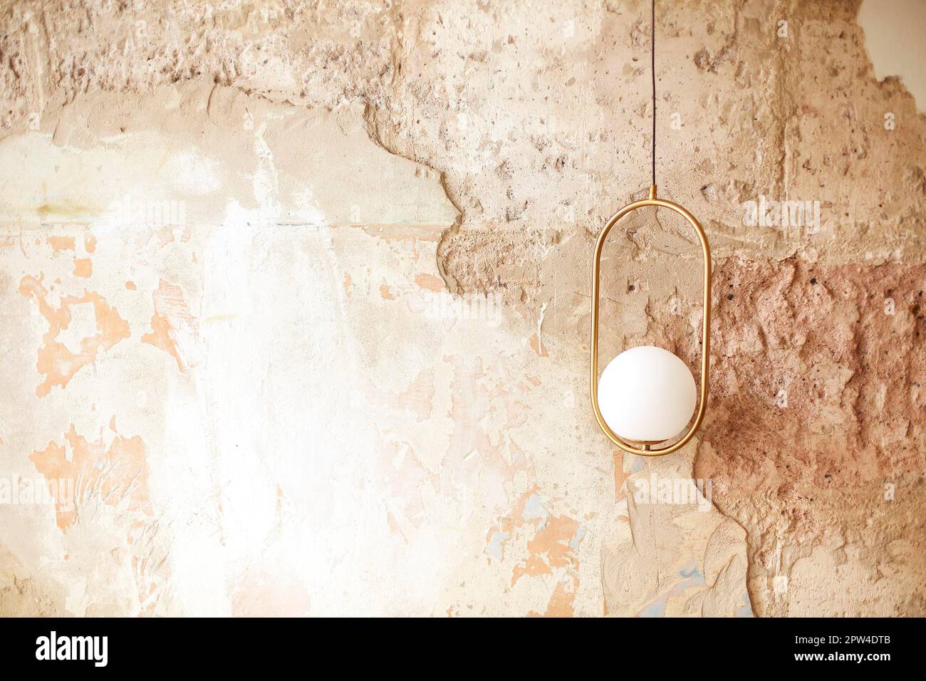 Trendy modern lamp with golden rim hanging against weathered concrete ...