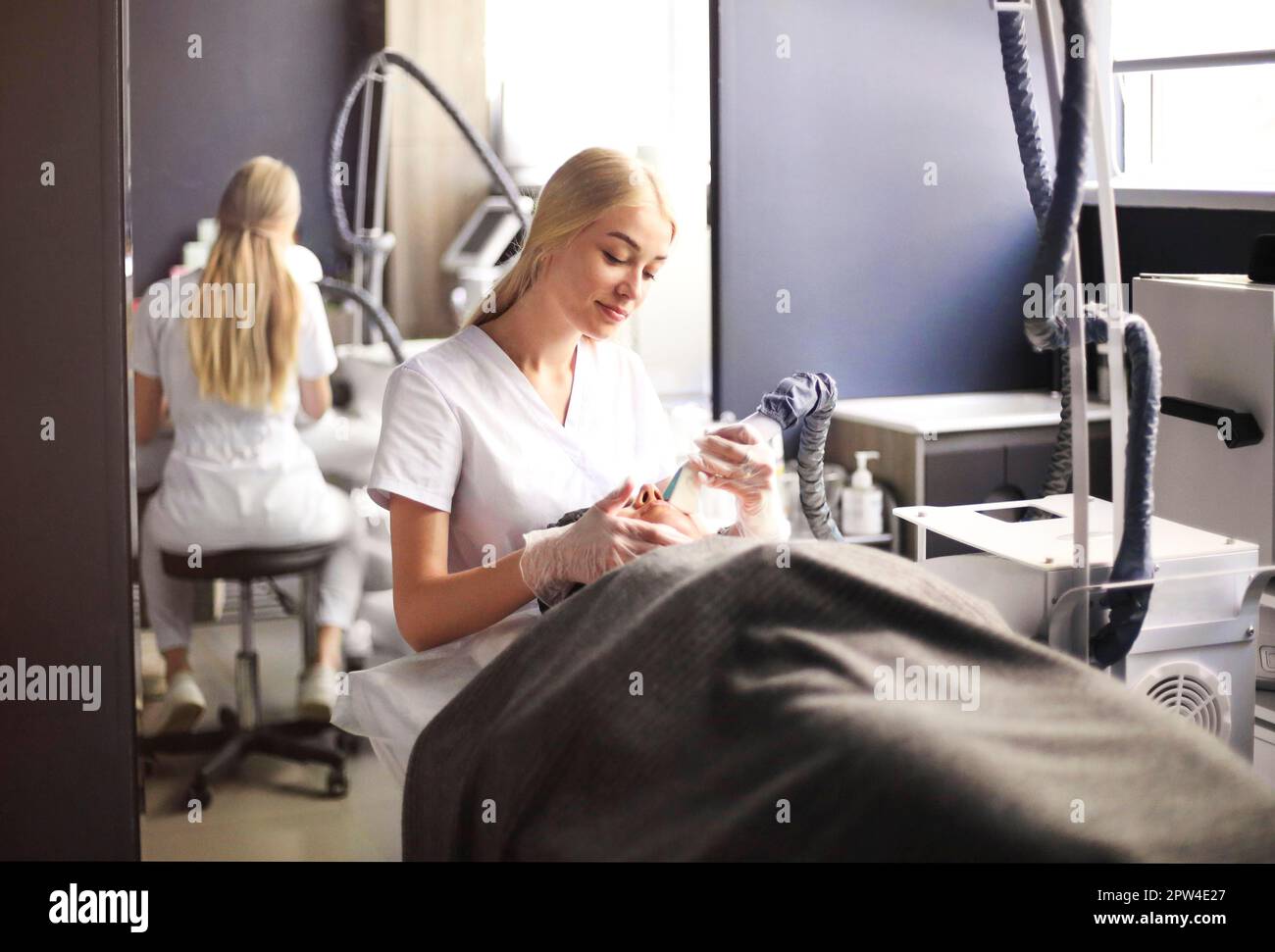 Female beautician in mask doing laser therapy procedure on face of ...